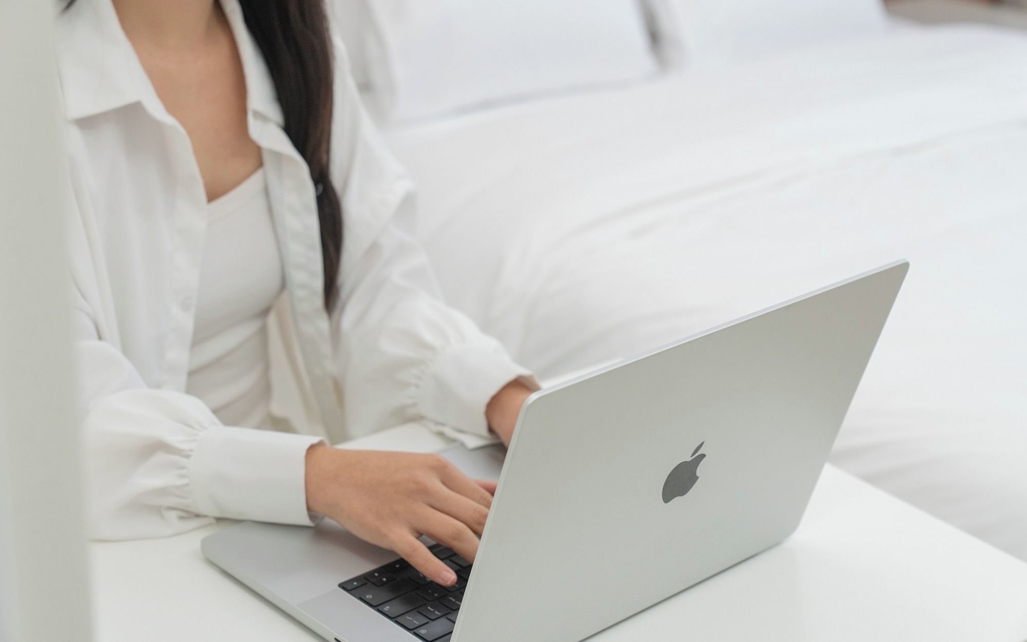 Uma pessoa usando um laptop em uma cama branca com roupa de cama branca.