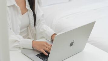Uma pessoa usando um laptop em uma cama branca com roupa de cama branca.