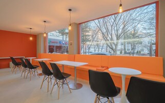 Um café moderno com assentos laranja, mesas brancas e cadeiras pretas.