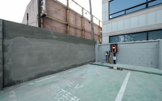 Uma área de estacionamento com um muro de concreto, um edifício de tijolos e um edifício moderno com grandes janelas.