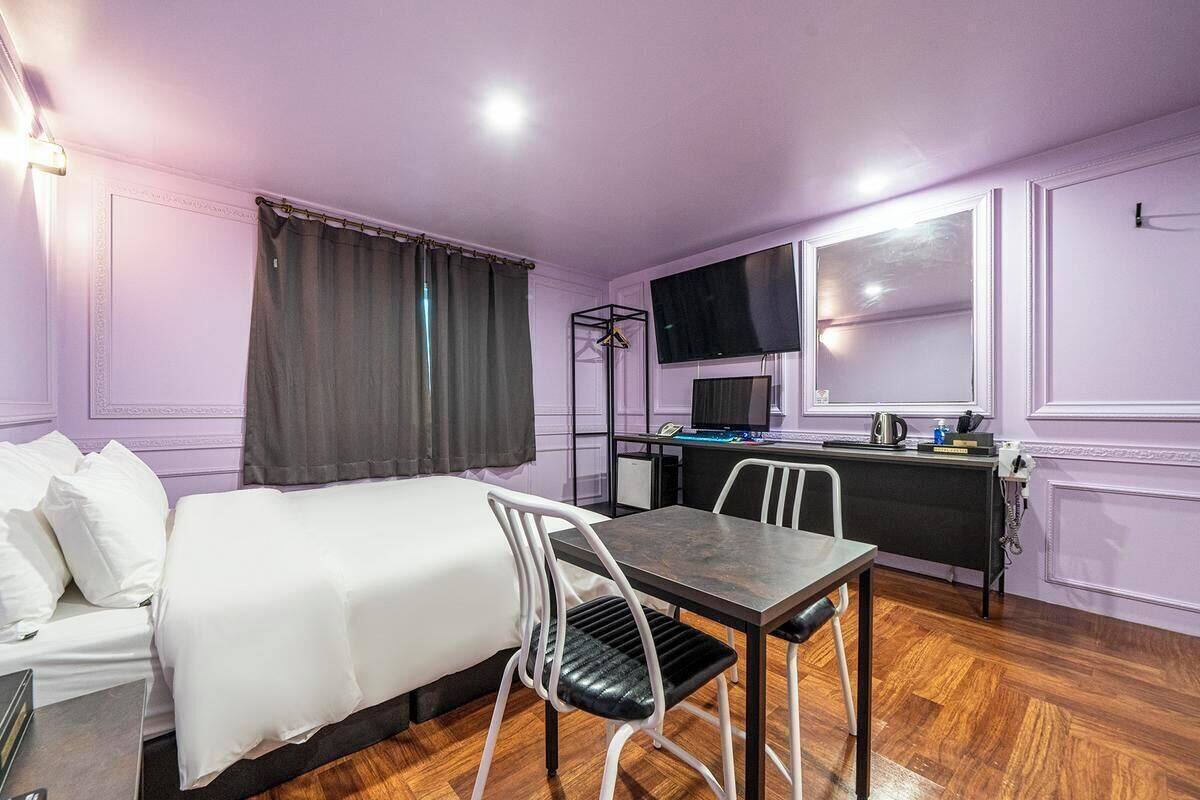 Quarto de hotel com cama, escrivaninha, cadeira, televisão e janela com cortinas.
