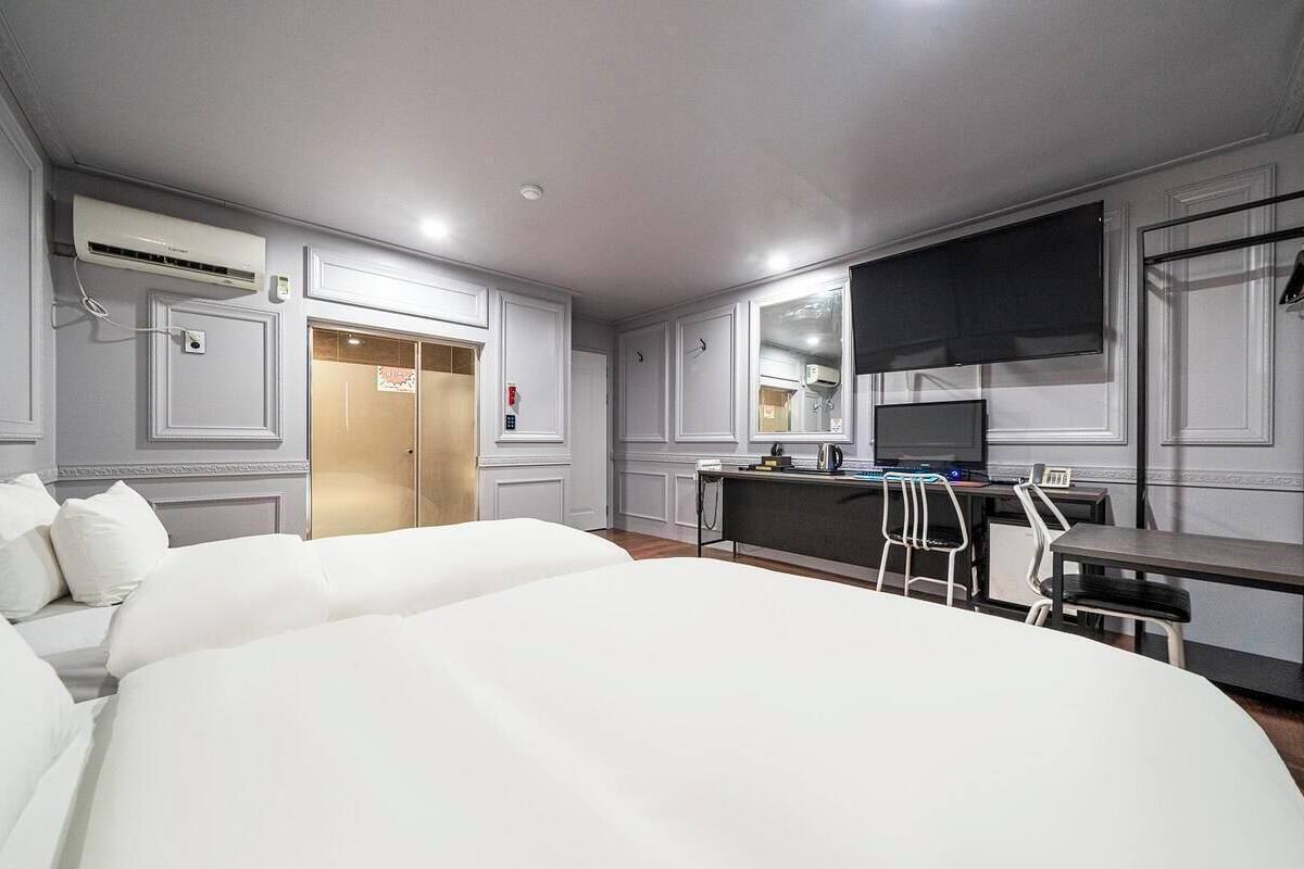 Quarto de hotel com uma cama grande, uma escrivaninha com cadeira, televisão e guarda-roupa.
