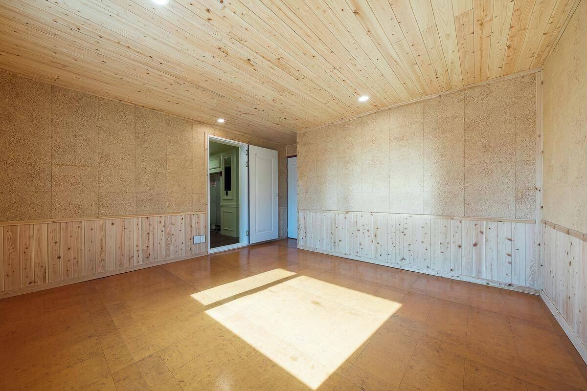 Um quarto espaçoso com paredes e teto de painéis de madeira, um amplo piso de madeira e uma porta que dá para outro cômodo.