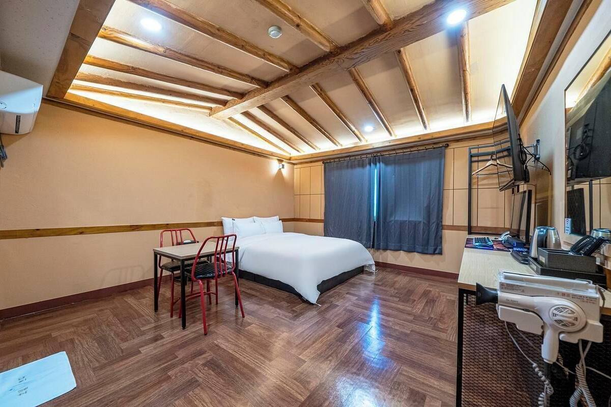 Quarto de hotel com teto de madeira, uma cama, uma escrivaninha com um computador e uma cadeira.