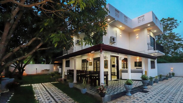 Uma casa moderna de dois andares com varanda coberta, área de estar externa e plantas em vasos.