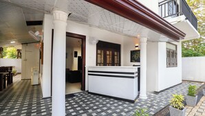 Uma área de recepção com balcão de check-in, piso em azulejos e uma varanda com guarda-corpo.