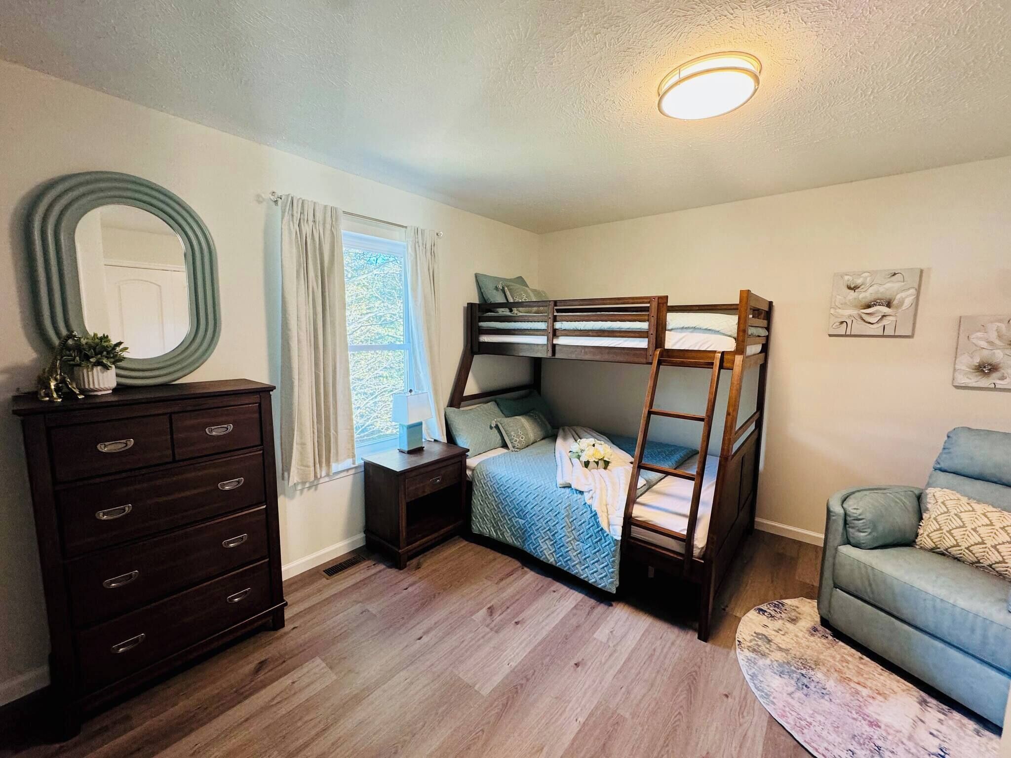 Quarto com uma cama de solteiro e solteira, cômoda, cadeira e janela com cortinas.
