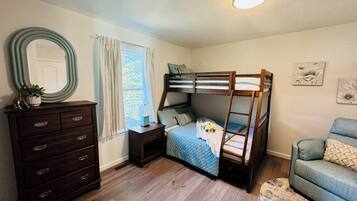 Quarto com uma cama de solteiro e solteira, cômoda, cadeira e janela com cortinas.