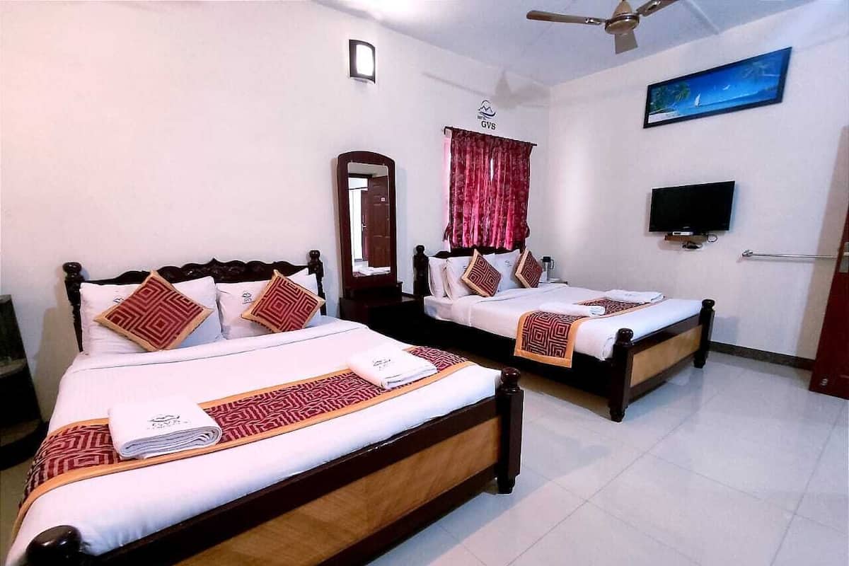 Quarto de hotel com duas camas, uma televisão, ventoinha no teto e janela com cortinas.