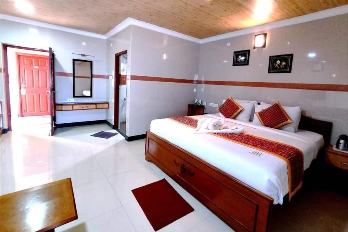 Quarto de hotel com teto de madeira, uma cama grande com roupa de cama branca, uma porta vermelha e uma pequena mesa.