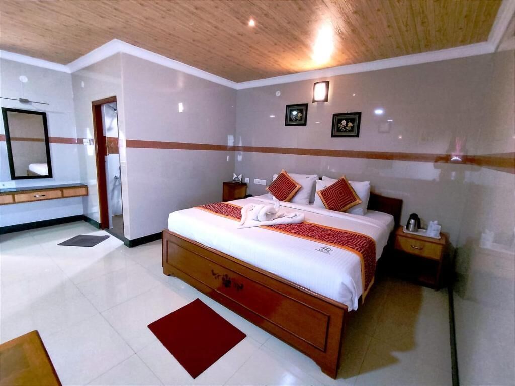 Quarto de hotel com uma cama de madeira, mesa de cabeceira, espelho e tapete vermelho.