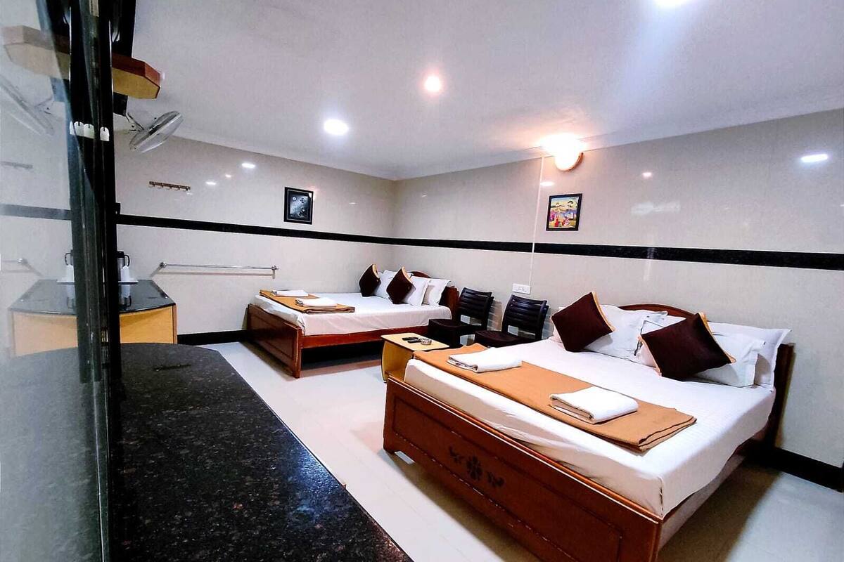 Quarto de hotel com duas camas, cômoda de madeira, mesa pequena e espelho.