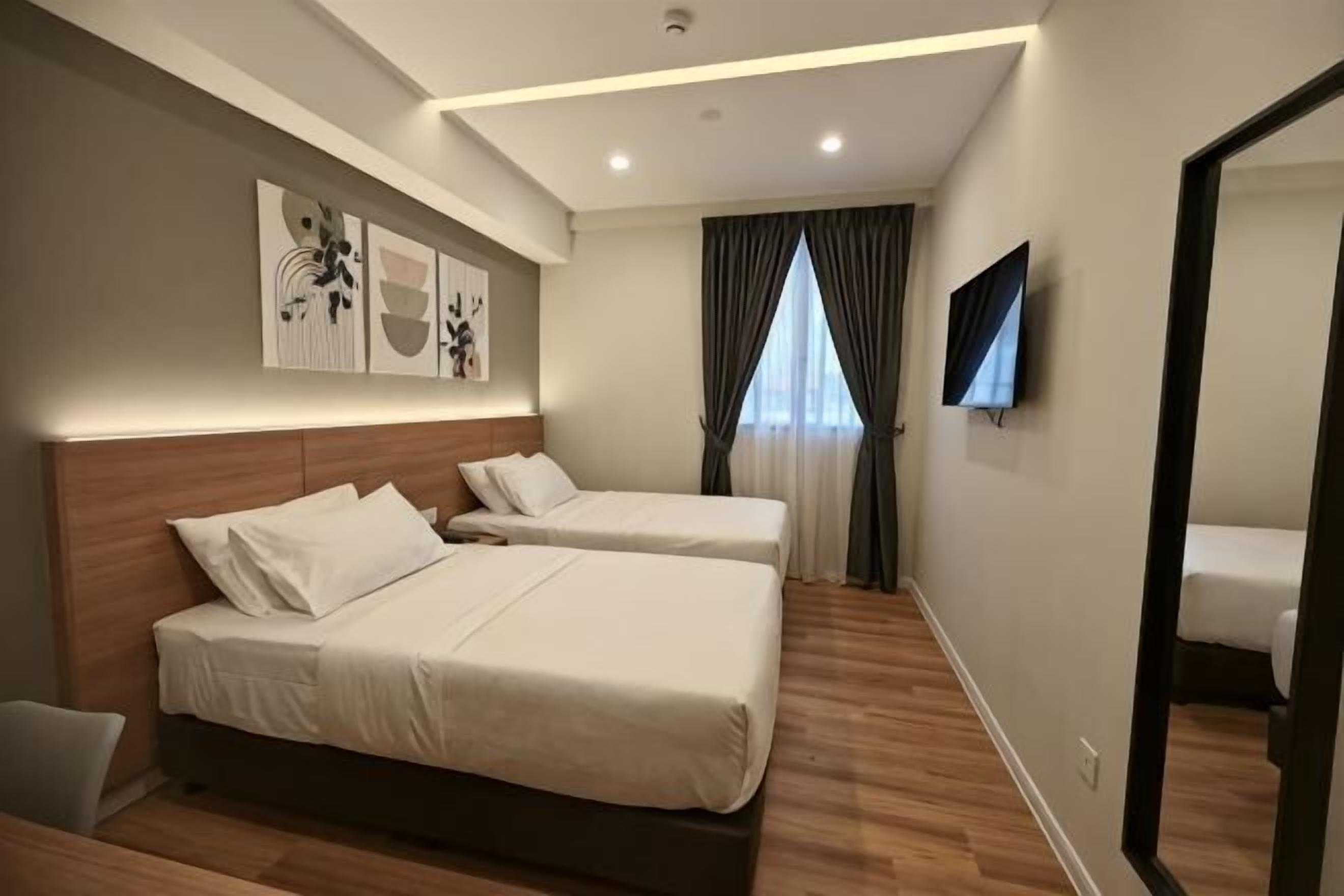 Quarto de hotel com duas camas, uma TV de tela plana, um espelho grande e uma janela com cortinas.