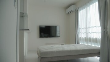 Quarto minimalista com cama, TV na parede e aparelho de ar condicionado.
