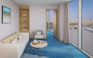 Quarto de hotel moderno com sofá, uma pequena mesa com bule, estante de livros e varanda com vista.