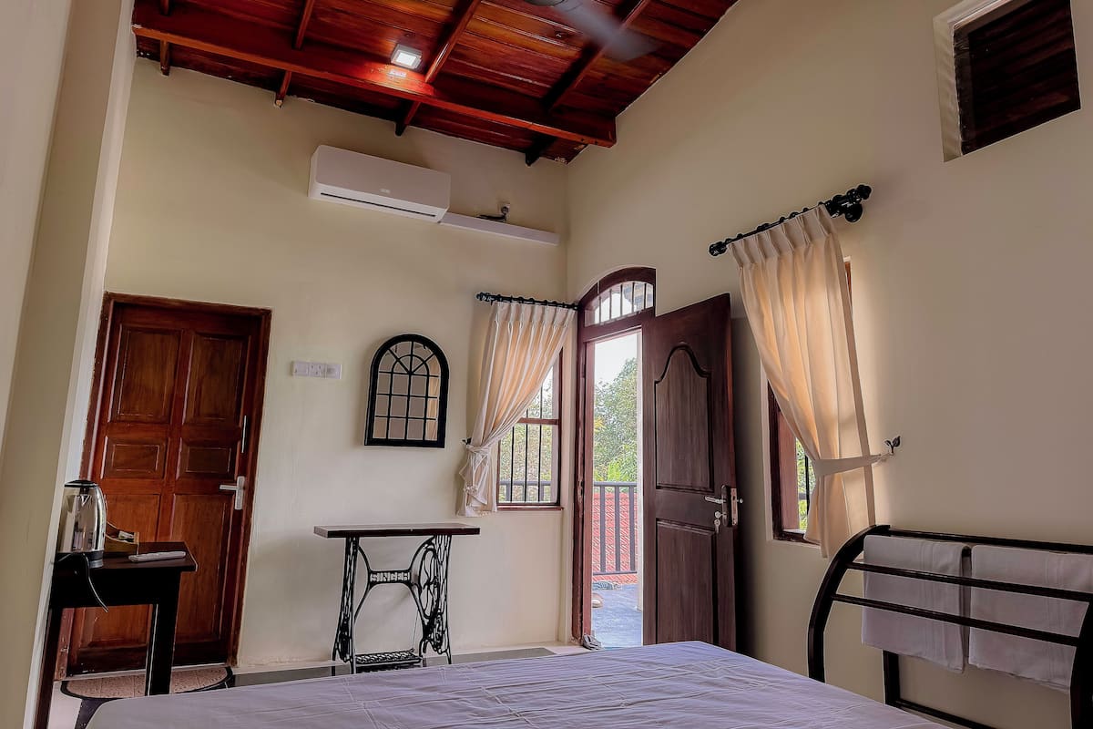 Um quarto com uma cama, uma máquina de costura, uma mesa, uma janela e uma porta.