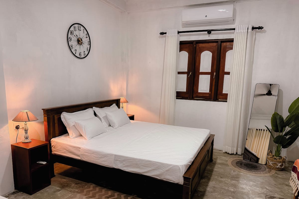 Cama bem arrumada com lençóis brancos, cabeceira de madeira e abajur em uma mesinha de cabeceira.