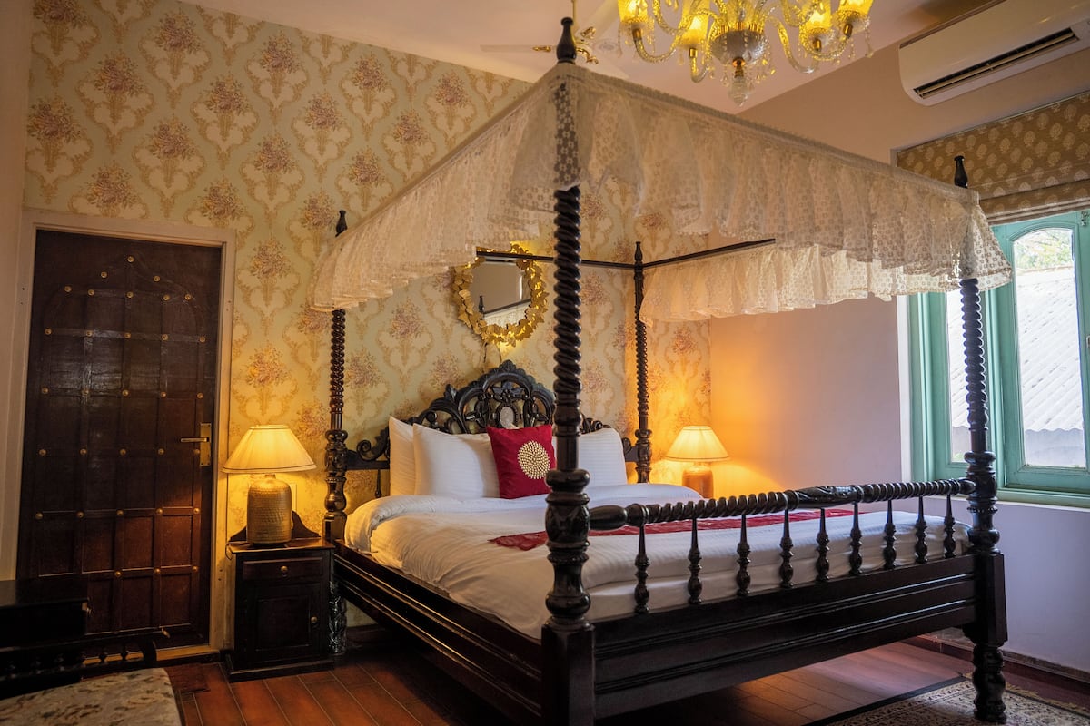 Uma cama com dossel e cortina, uma porta de madeira e uma janela com vista.