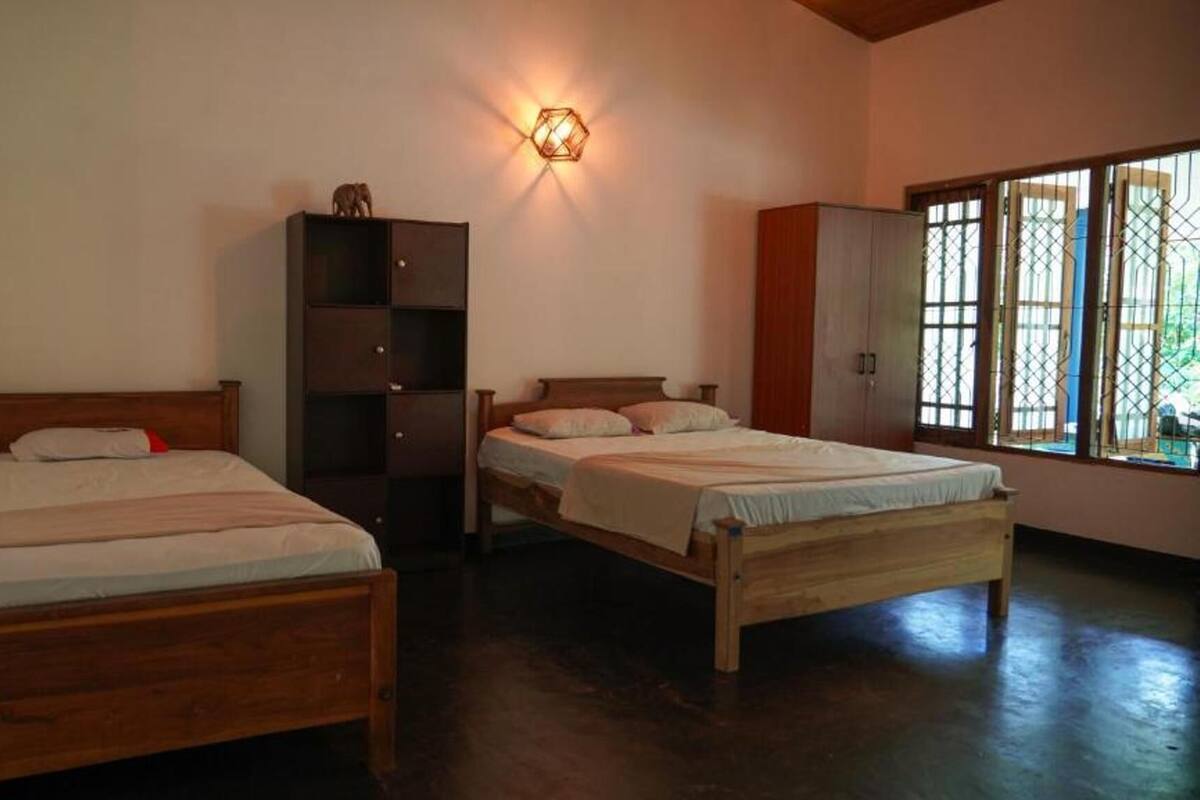 Quarto com duas camas de madeira, um guarda-roupa e uma janela com grades.