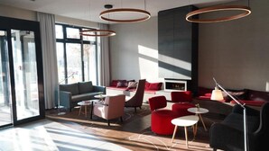 Uma área de estar moderna com um sofá, poltronas e pufes vermelhos. Há luminárias pendentes e uma lareira.