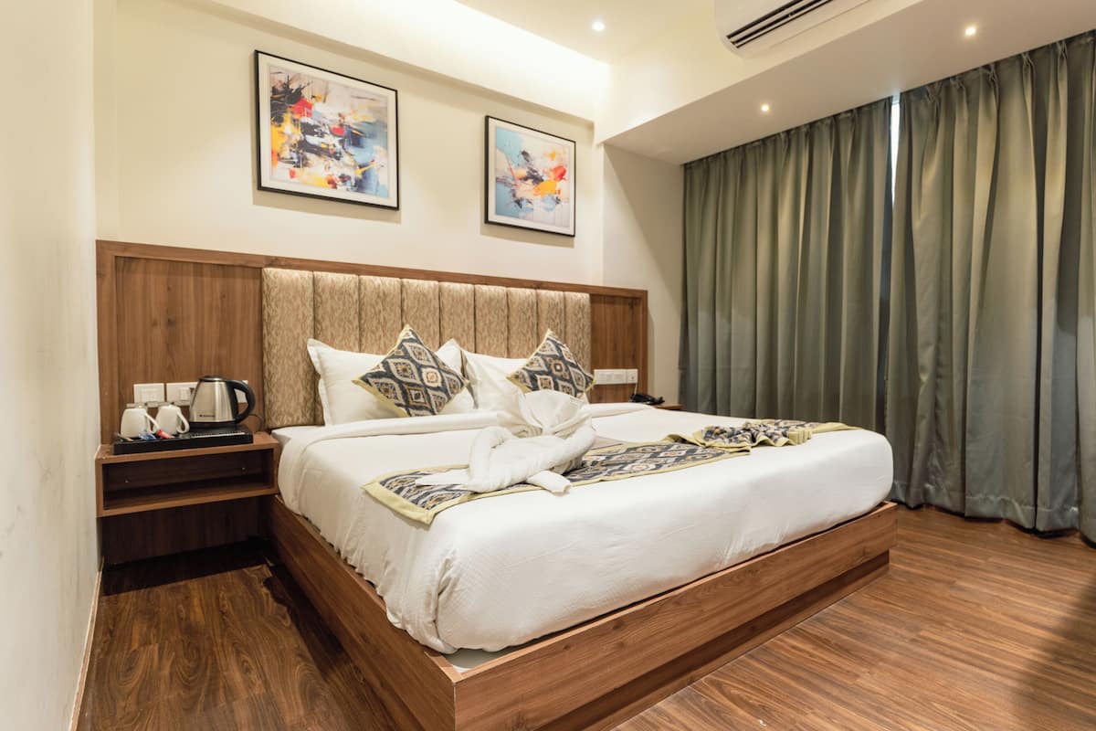 Quarto de hotel moderno com estrutura de cama de madeira, mesa de cabeceira com chaleira e duas pinturas abstratas na parede.