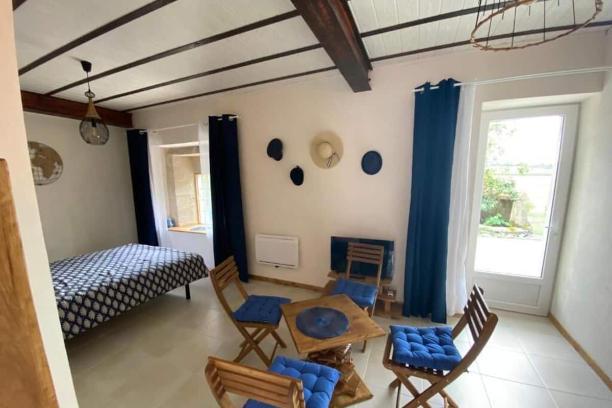 Quarto com cama, mesa de jantar com cadeiras e janela com cortinas.