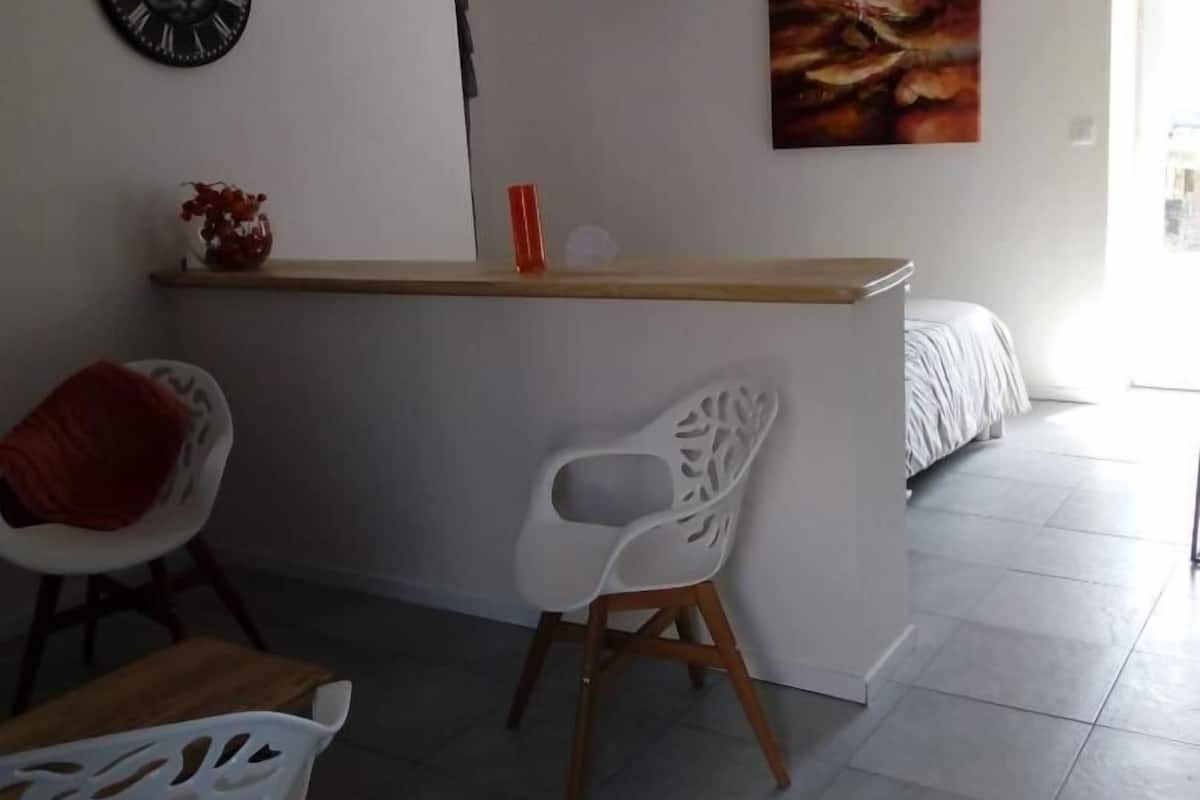 Cozinha moderna com ilha central, cadeiras brancas, um relógio e um quadro na parede.