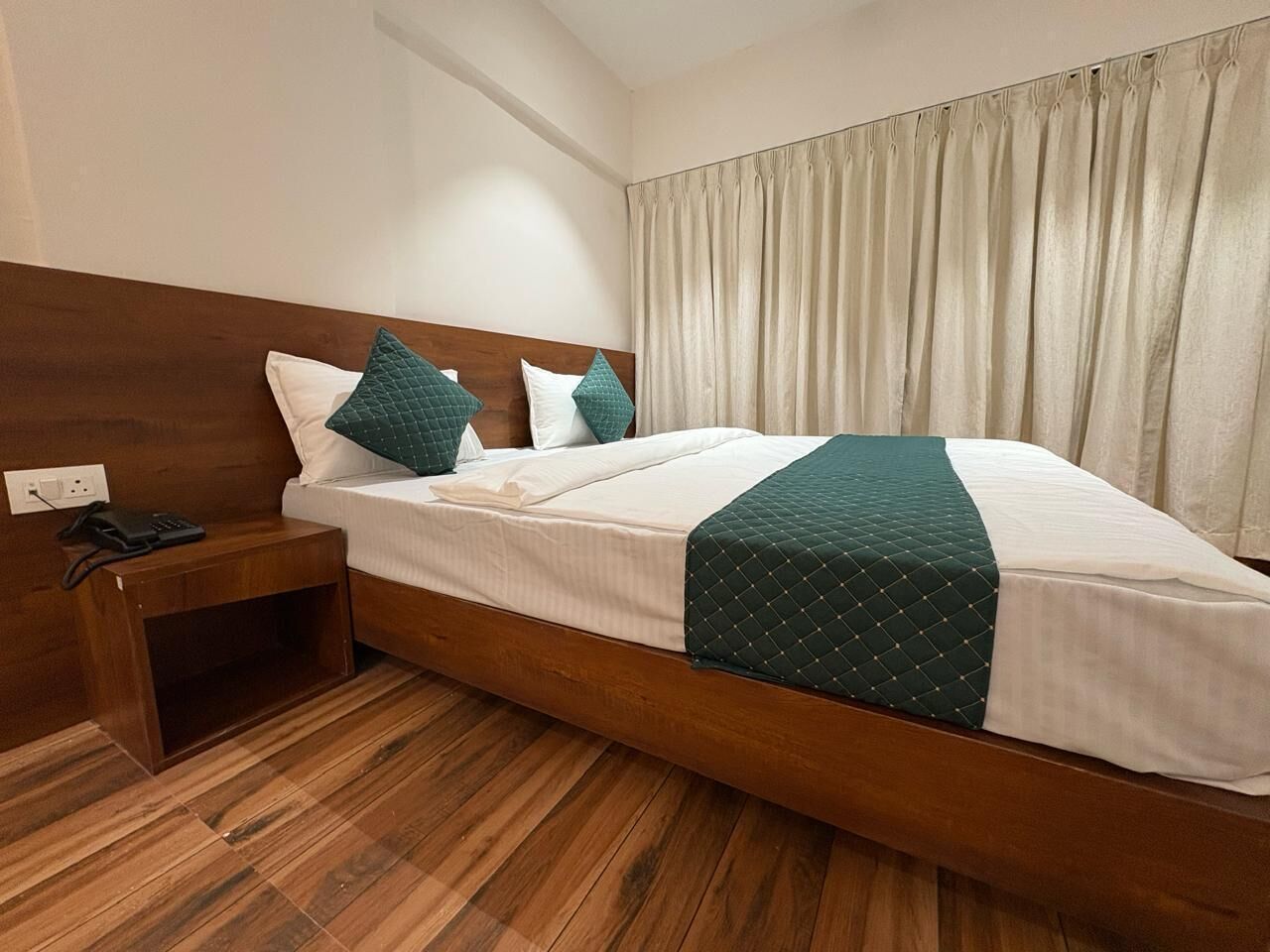 Quarto de hotel com cama de madeira, roupa de cama branca e manta acolchoada verde.