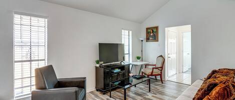 Uma sala de estar com sofá de couro, mesa de centro de vidro, televisão de tela plana e lareira.
