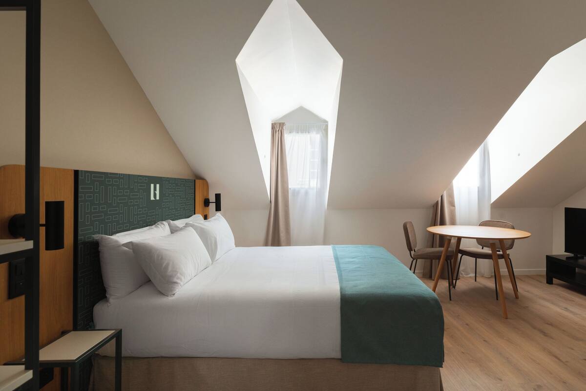 Quarto de hotel moderno com uma cama, escrivaninha, cadeira e televisão.