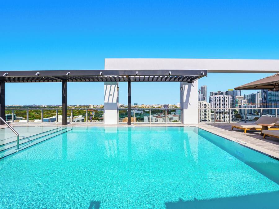 Uma piscina no terraço com água azul cristalina, uma pérgula, cadeiras de descanso e vista para o horizonte da cidade.