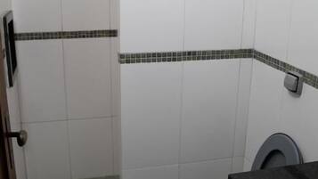 Casa de banho com sanita, bidé e lavatório. Tem uma janela com estrutura preta e uma persiana amarela. As paredes estão revestidas com azulejos brancos e verdes.