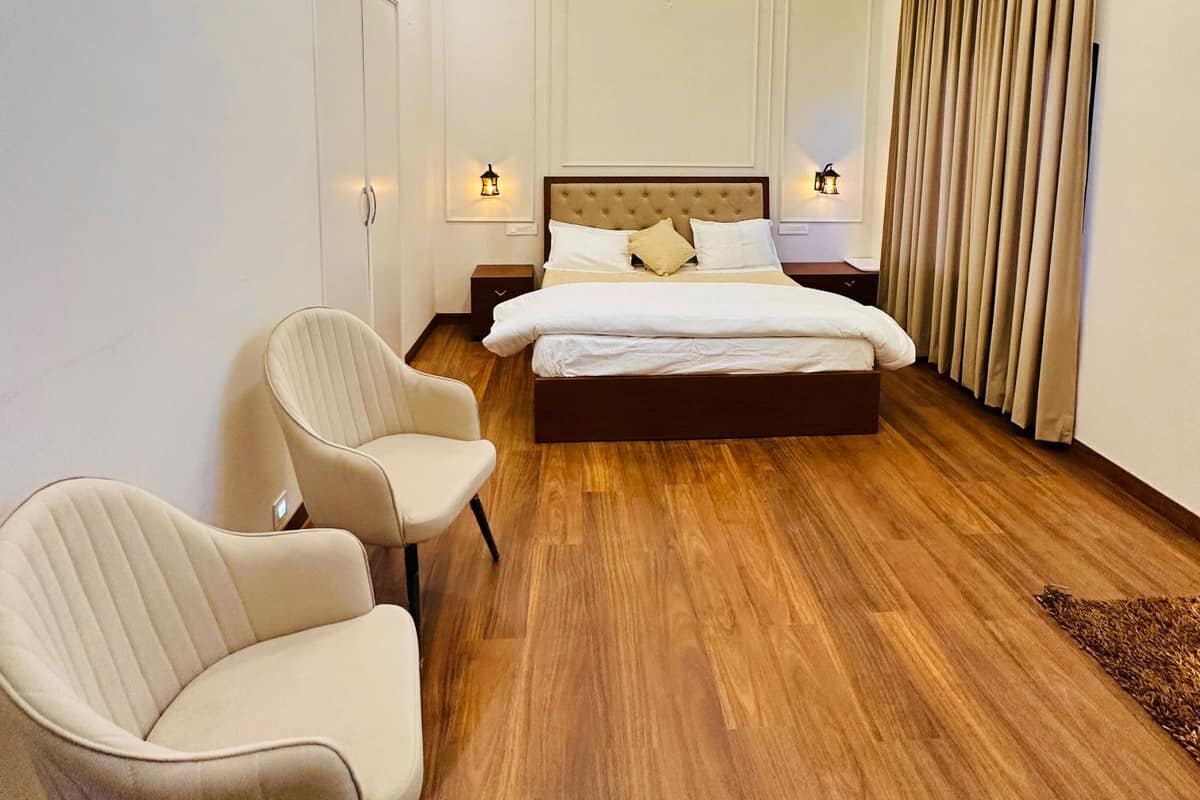 Quarto de hotel moderno com uma cama grande, duas mesas de cabeceira, uma cadeira e piso de madeira.