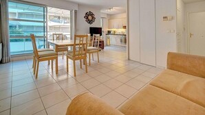 Uma sala de estar moderna com sofá, mesa de jantar, cadeiras e cozinha ao fundo.