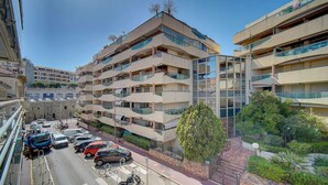 Um edifício residencial com várias andares, varandas, área de estacionamento e um pequeno jardim.