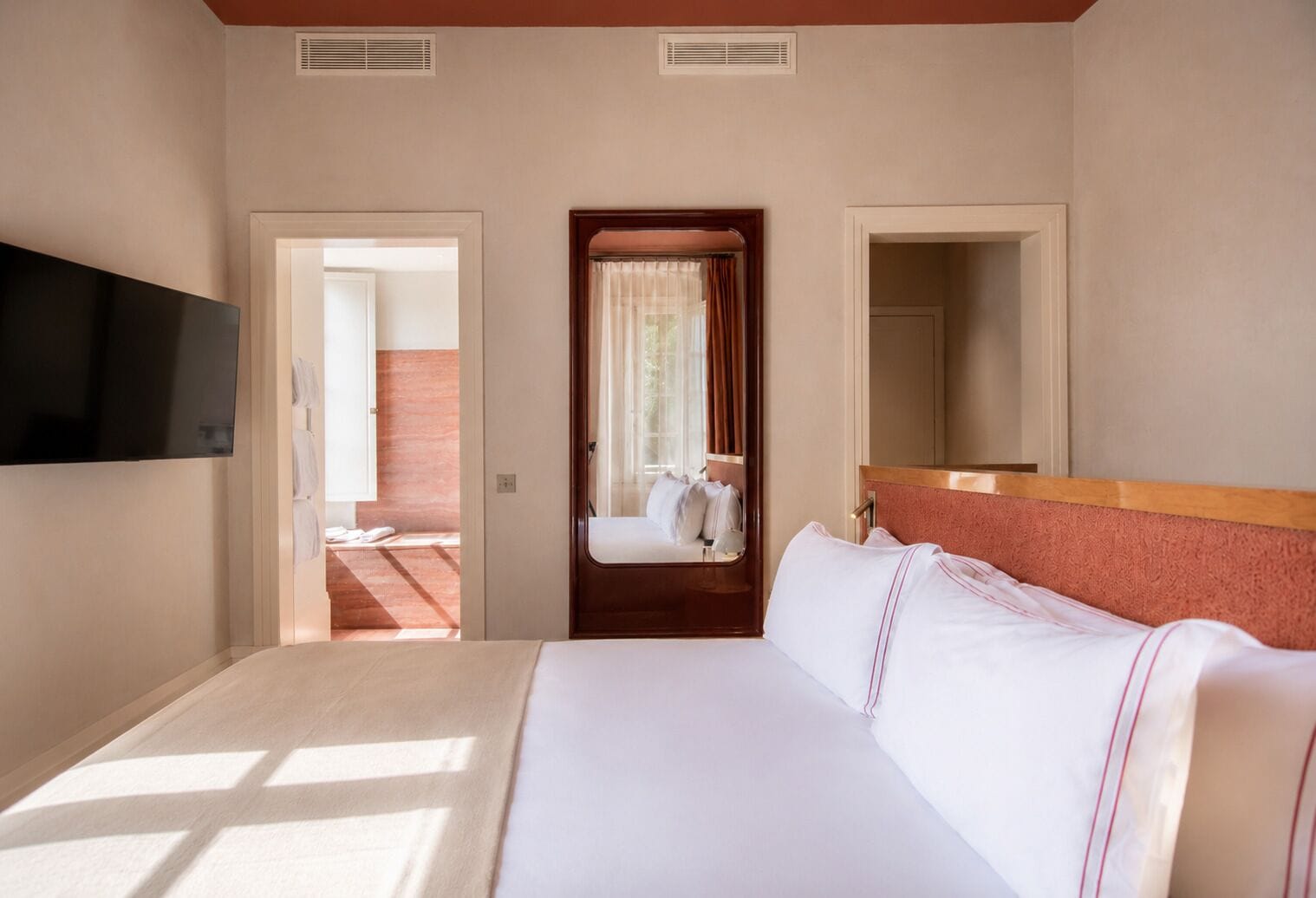 Quarto de hotel com cama, televisão, banheiro com espelho e porta que dá para uma área externa.
