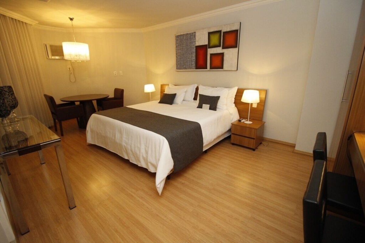 Quarto de hotel com cama, mesas de cabeceira, escrivaninha e uma cadeira.