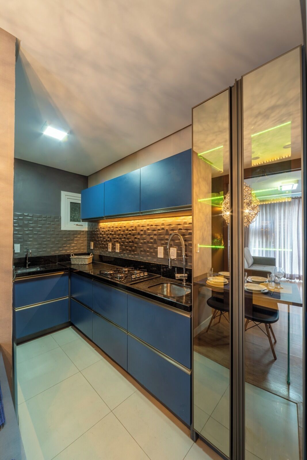 Uma cozinha moderna com armários azuis, bancada preta e divisória de vidro.