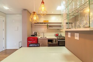 Cozinha moderna com bancada branca, cafeteira vermelha PHILCO, fogão a gás e luminárias pendentes.