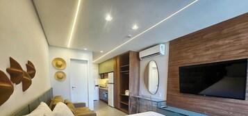 Quarto de hotel moderno com cama, televisão, guarda-roupa, secretária e cozinha compacta.