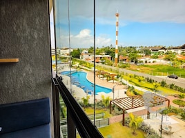 Vista de um quarto de hotel com piscina, área de estar externa e uma torre de comunicação alta ao fundo.
