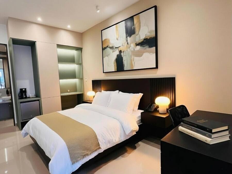 Quarto de hotel moderno com uma cama grande, mesas de cabeceira, uma escrivaninha e uma pintura abstrata pendurada na parede.