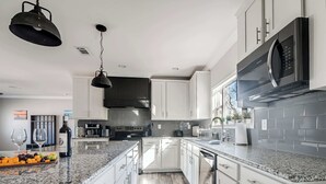 Uma cozinha moderna com armários brancos, bancadas de granito, exaustor preto e micro-ondas embutido.