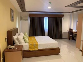Quarto de hotel com cama, mesa de cabeceira e escrivaninha com cadeira.