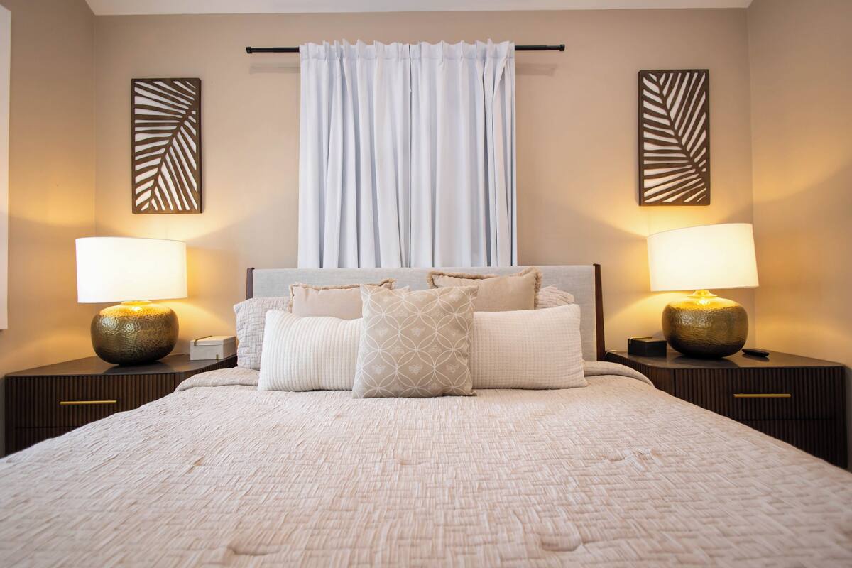 Cama bem arrumada com manta texturizada, duas luminárias de cabeceira e decoração na parede.