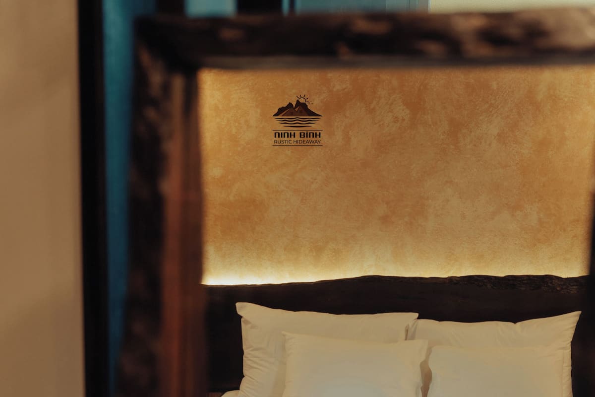Uma cama com lençóis brancos, cabeceira de madeira e um espelho refletindo uma cama com lençóis brancos.
