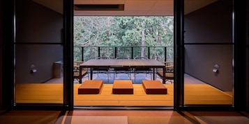 Visão do interior de um quarto com piso de madeira, uma mesa com cadeiras e um banco.