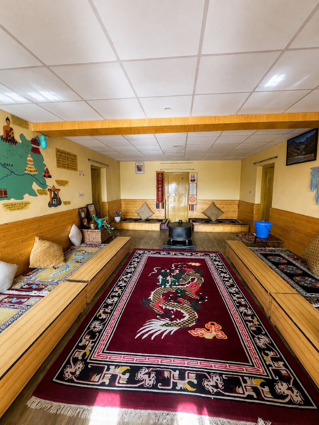 Quarto com um tapete central com design de dragão, bancos de madeira ao longo das paredes e um mapa na parede esquerda.