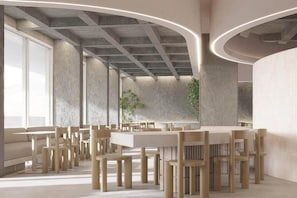 Um interior moderno com uma mesa de jantar central rodeada de cadeiras, tetos altos com vigas aparentes e amplas janelas que permitem a entrada de luz natural.