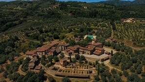 Vista aérea de uma aldeia rural com edifícios de pedra tradicionais, campos em socalcos e uma moradia imponente com piscina.
